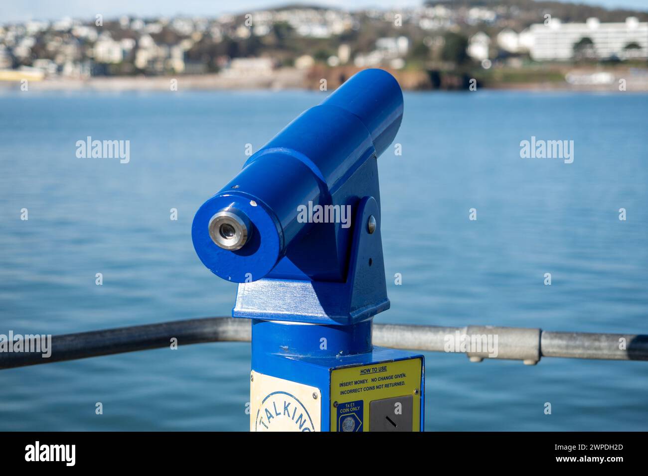 A blue viewing telescope looks out over a calm blue sea towards land at ...