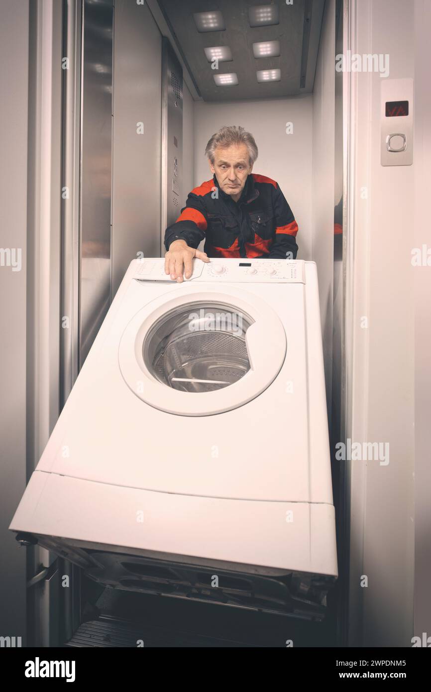 Older man in overall moving wash machine on cart with elevator Stock ...