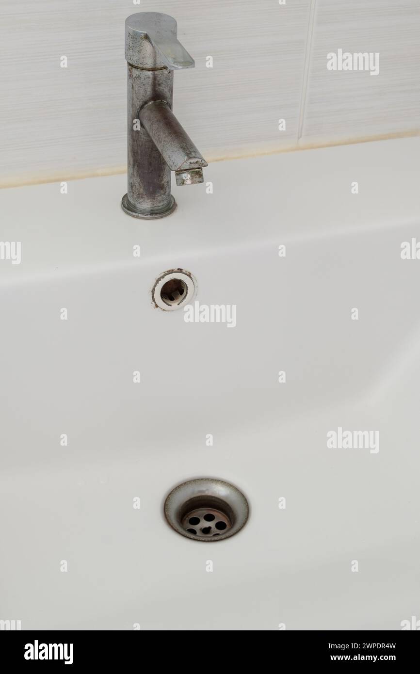The ceramic sink basin with the stained faucet near the white tile wall ...