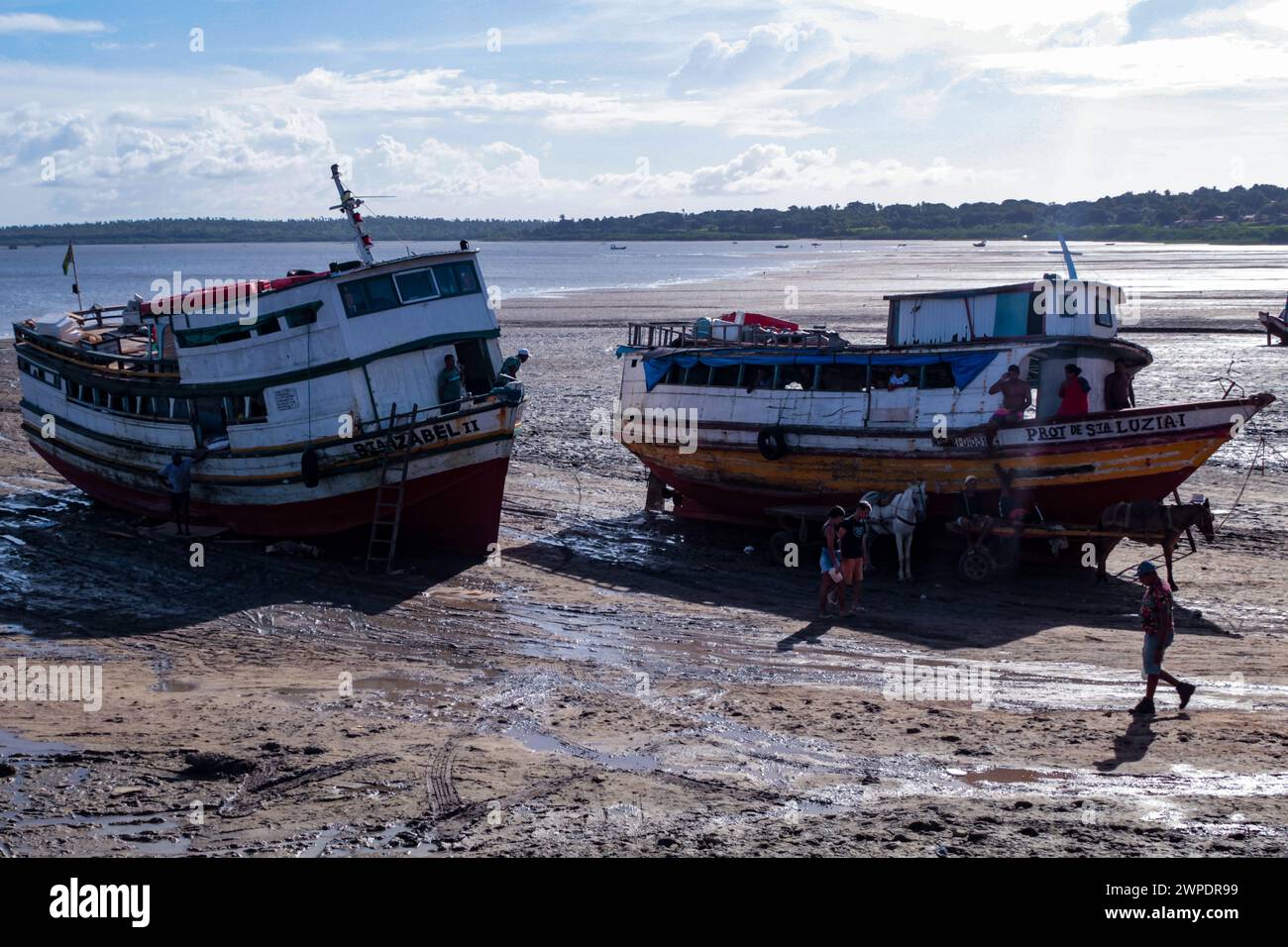 Some people, a cart and wooden boats, stranded on Barbosa beach, in São ...
