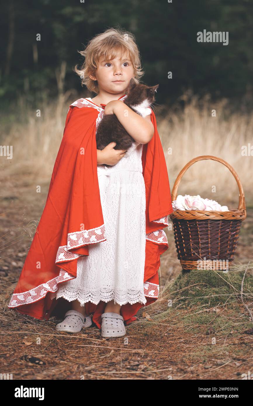 Little red riding hood with basket of food posing with kitten in forest ...