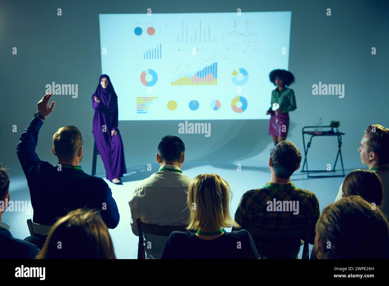 Conference presentation with woman in purple hijab gesturing to chart ...