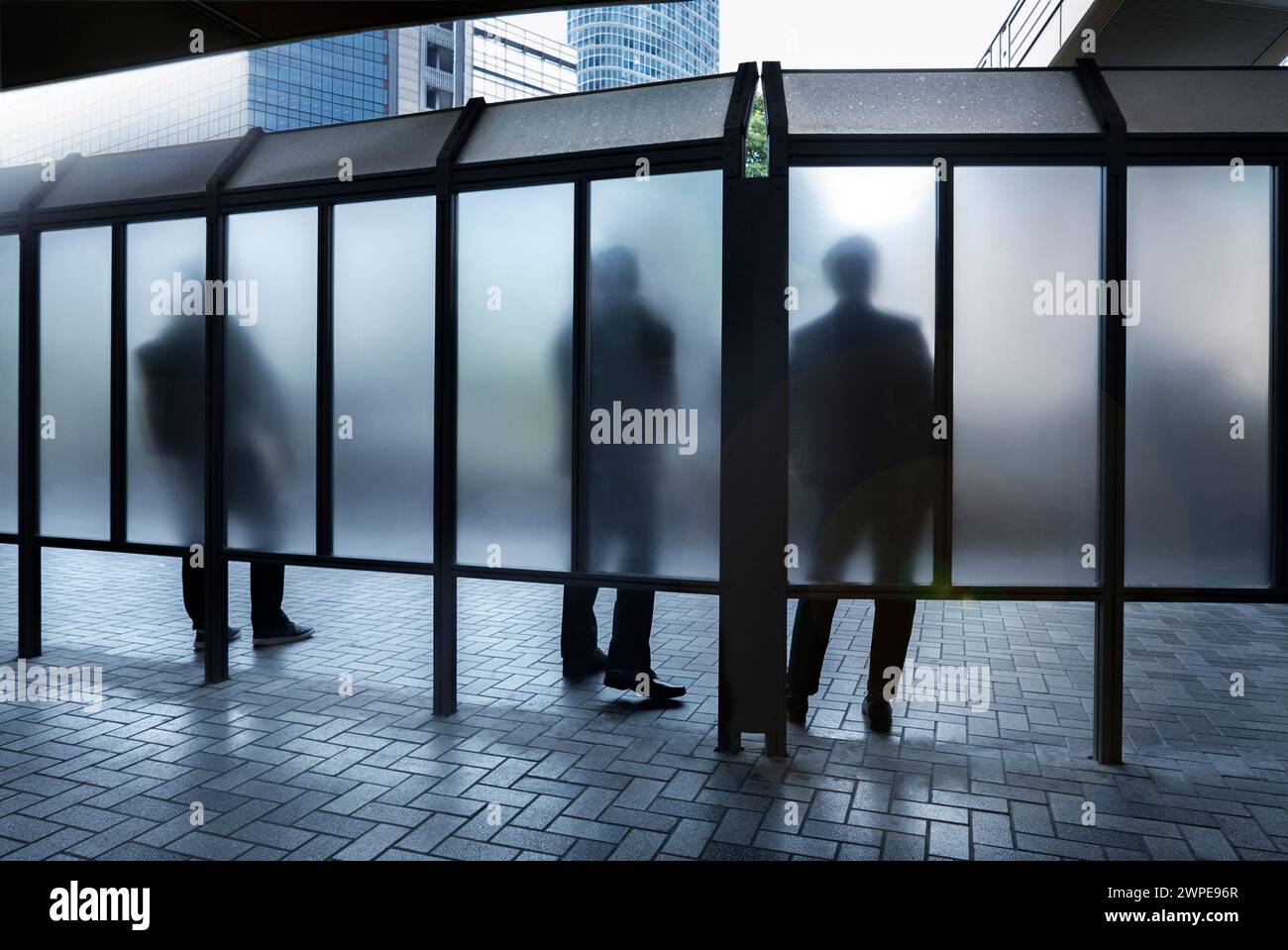 City scene of people stood behind frosted glass at urban shelter or bus ...