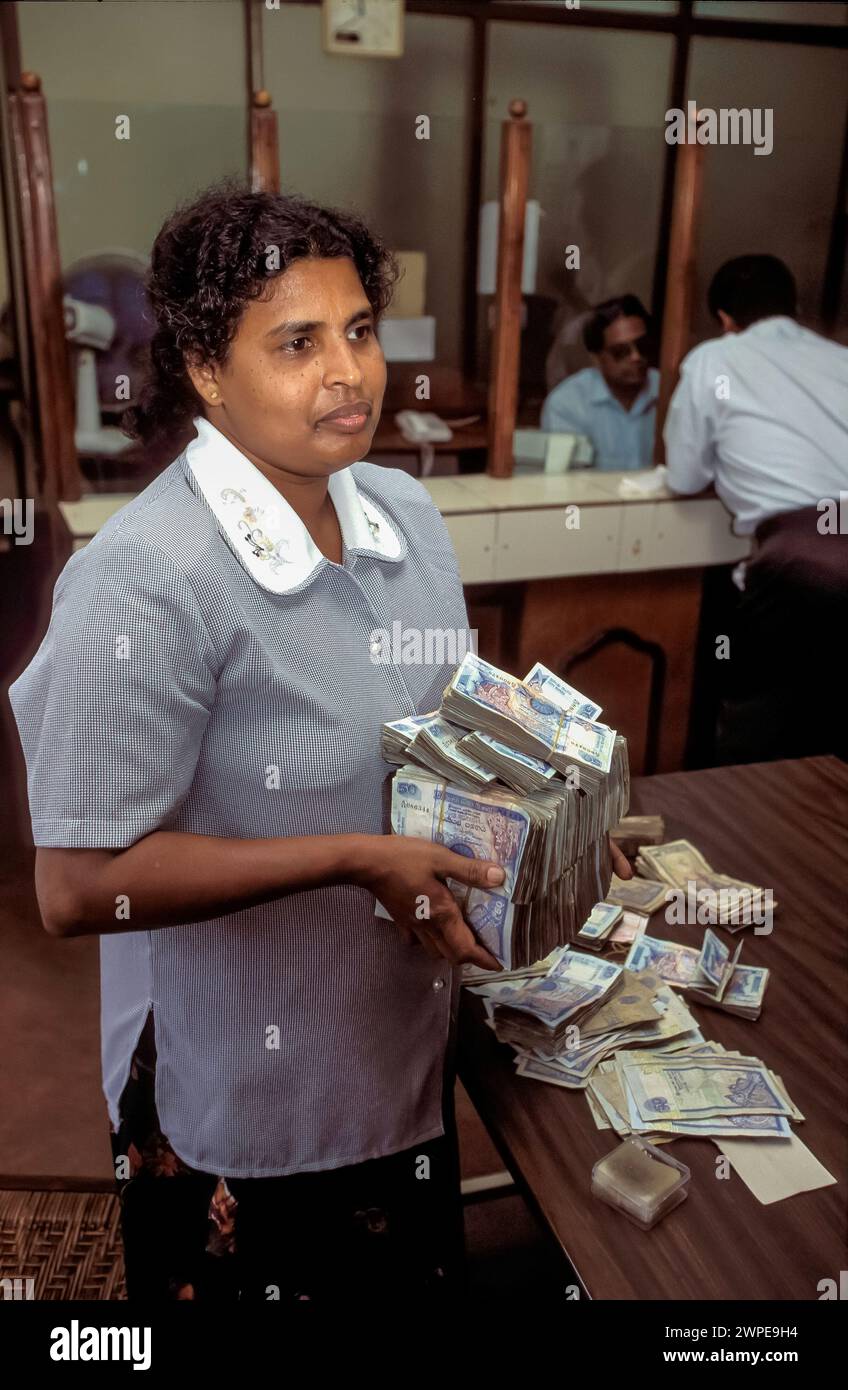 Sri Lanka, Colombo, a female bank employee holding packs of paper money ...