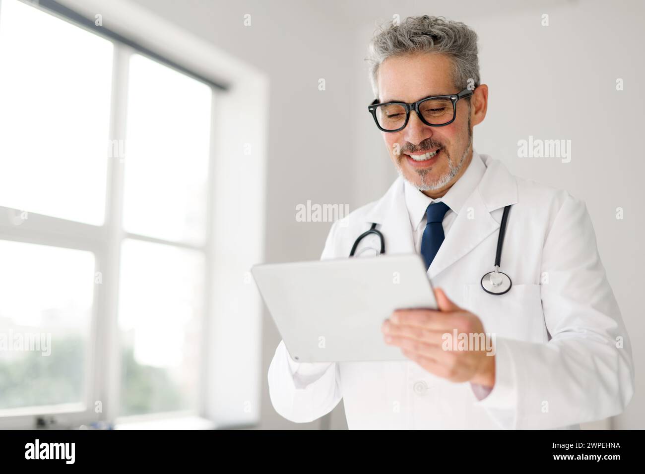 A cheerful senior doctor with grey hair and spectacles reviews ...