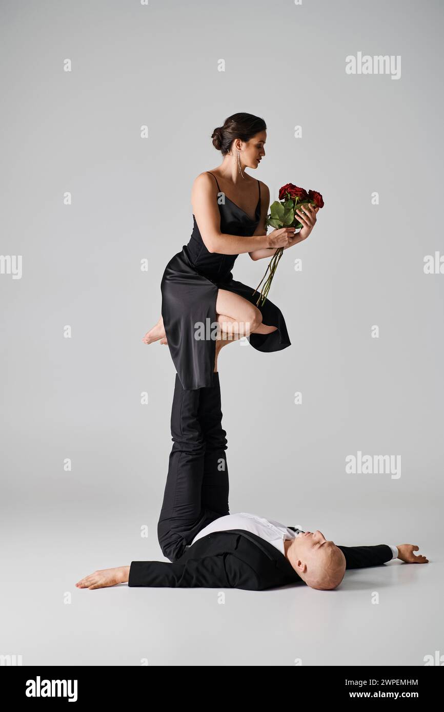 acrobatic woman in black dress holding red roses and balancing on feet ...
