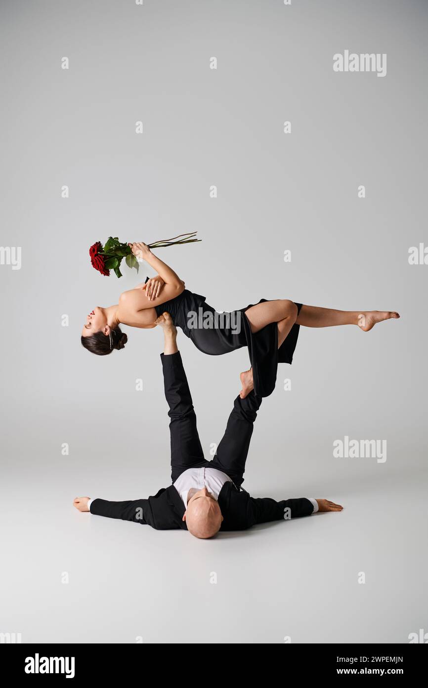 flexible woman in black attire holding red roses and balancing on feet ...