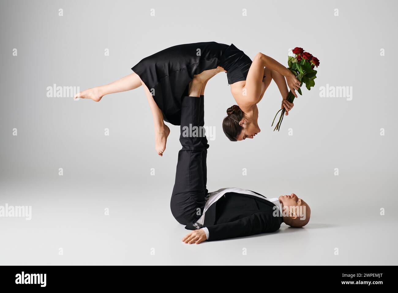 flexible woman in black dress holding red roses and balancing on feet ...