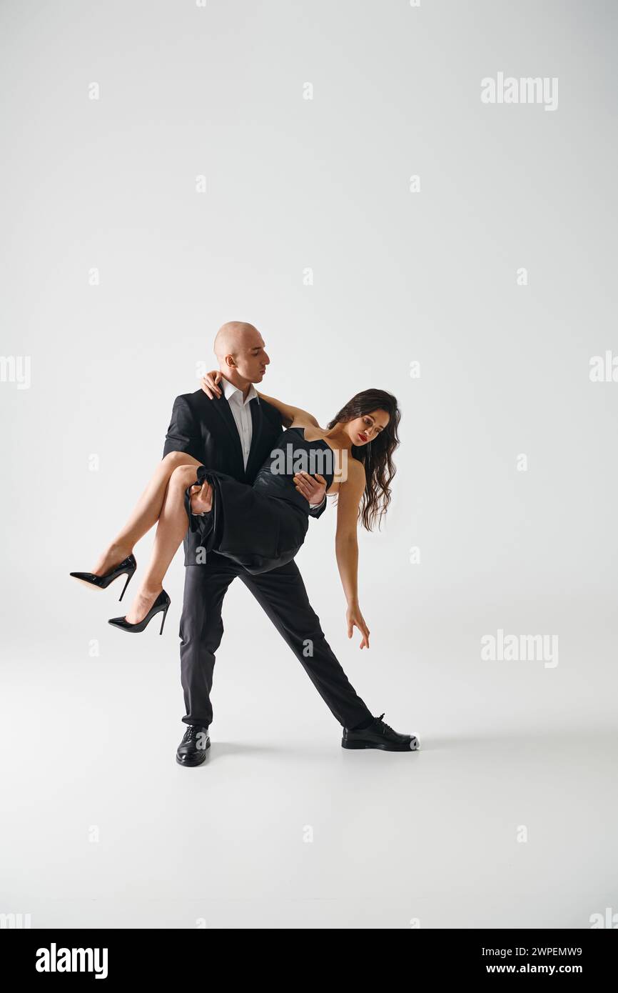 strong man carrying young elegant woman in black dress and high heels ...