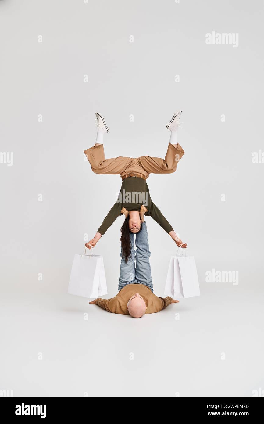 artistic couple, acrobatic woman holding shopping bags and balancing ...