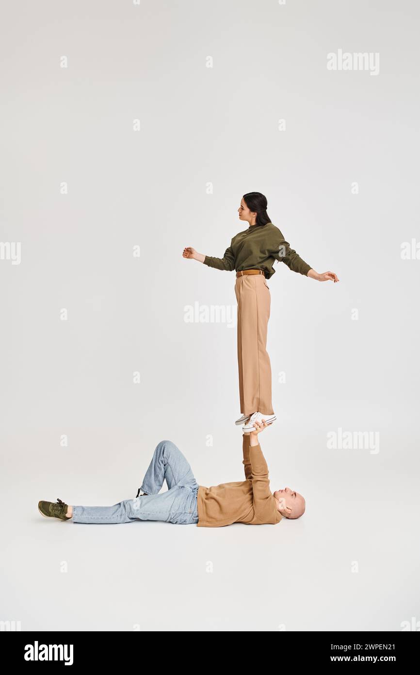 young brunette woman in casual wear balancing on hands of strong man ...