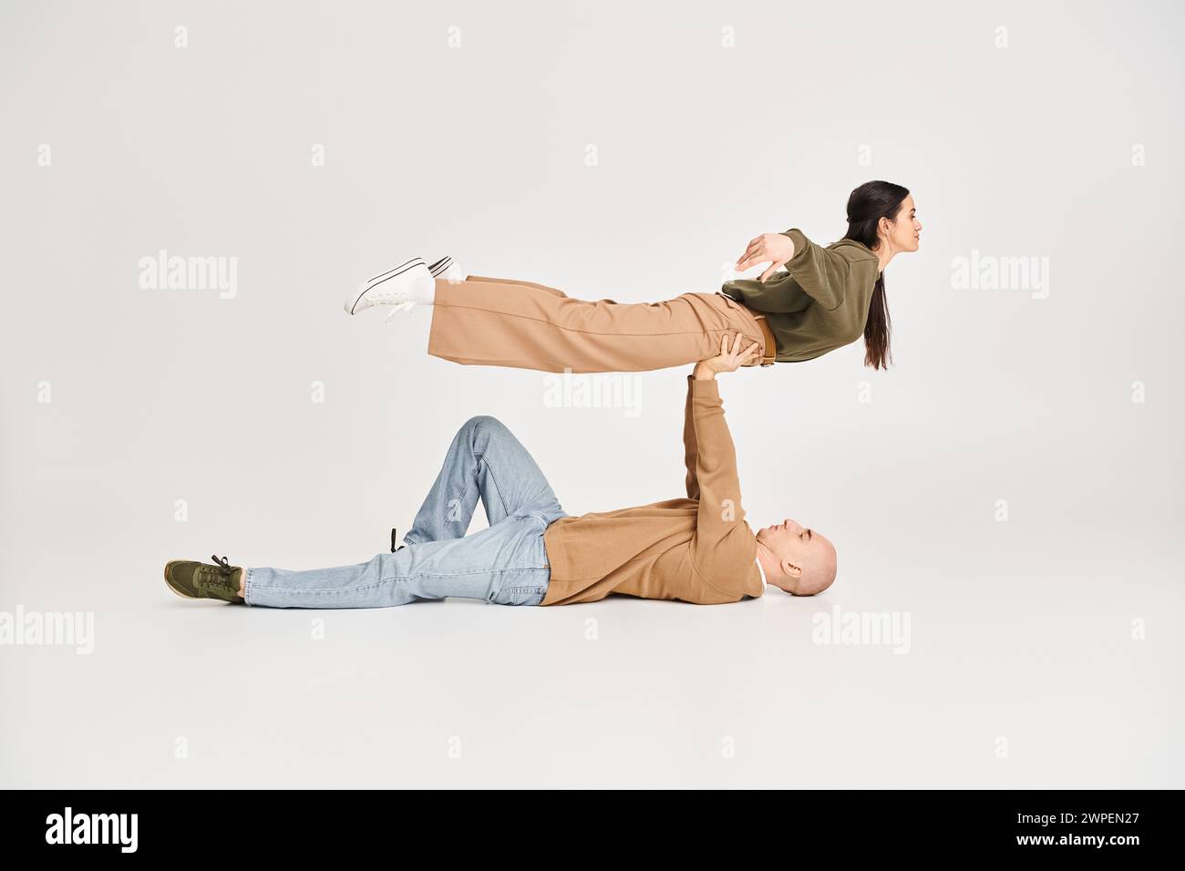 strong man in casual wear lying on floor and lifting brunette woman in ...
