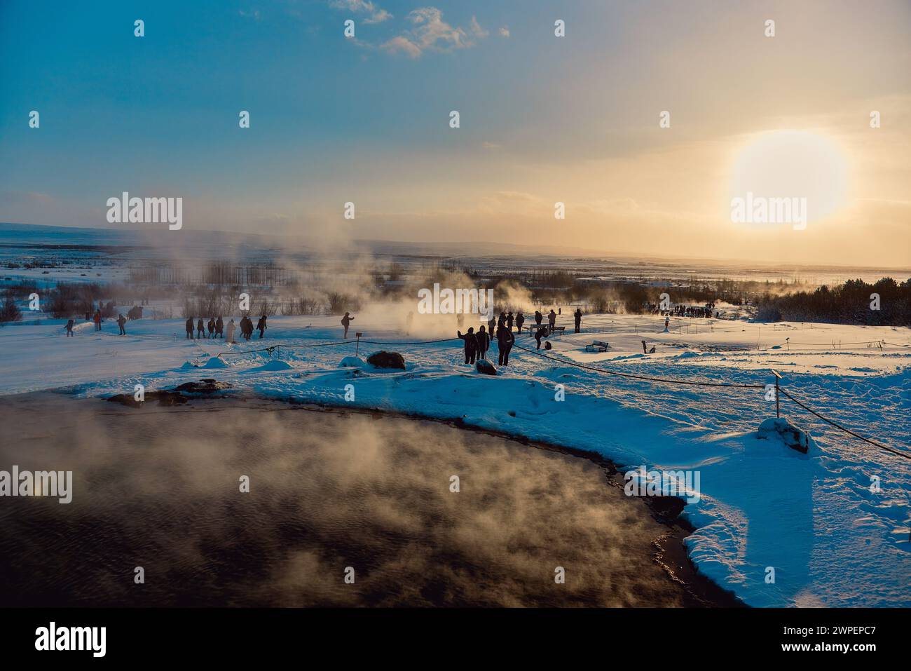 Winter landscape with geothermal springs, tourists, and a setting sun ...