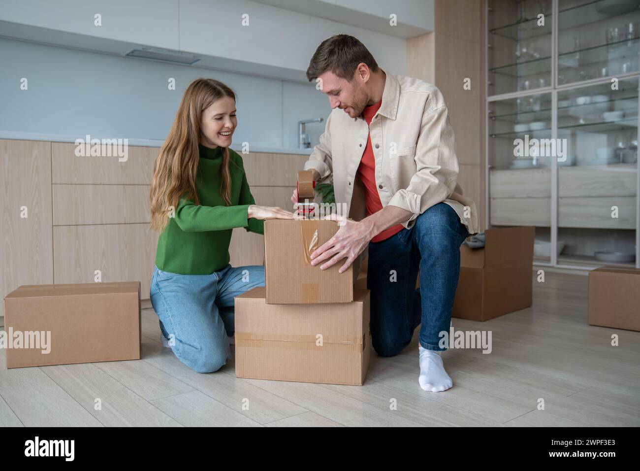 Positive couple packing things into cardboard boxes preparing to move ...