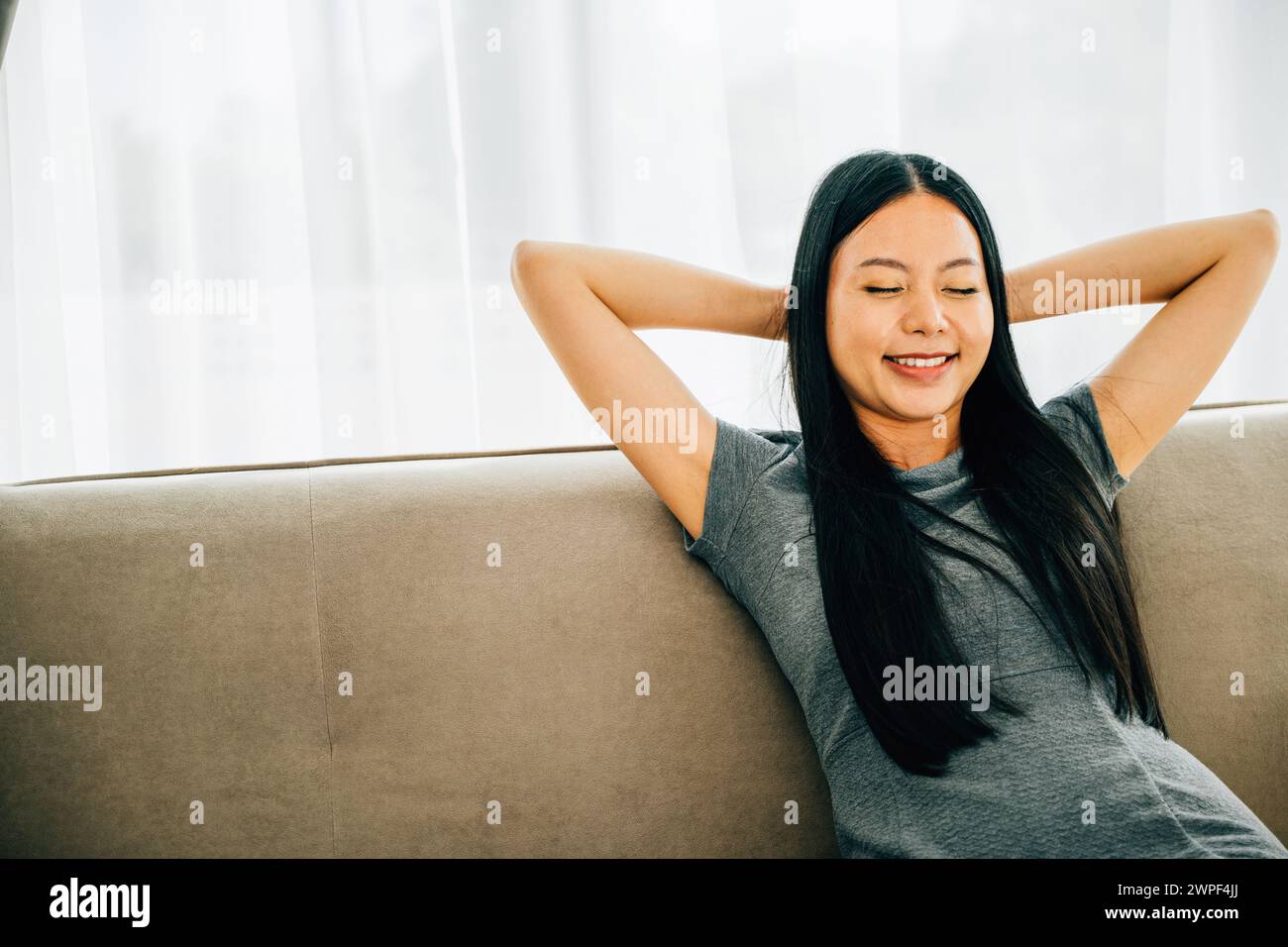 Relaxed woman on sofa hands behind head enjoys serene moment Stock ...