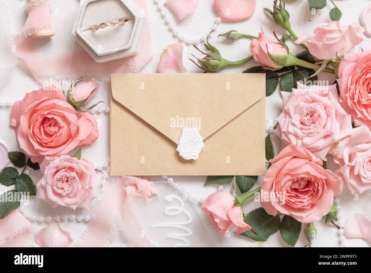 Kraft paper sealed envelope near light pink roses, engagement ring in a ...
