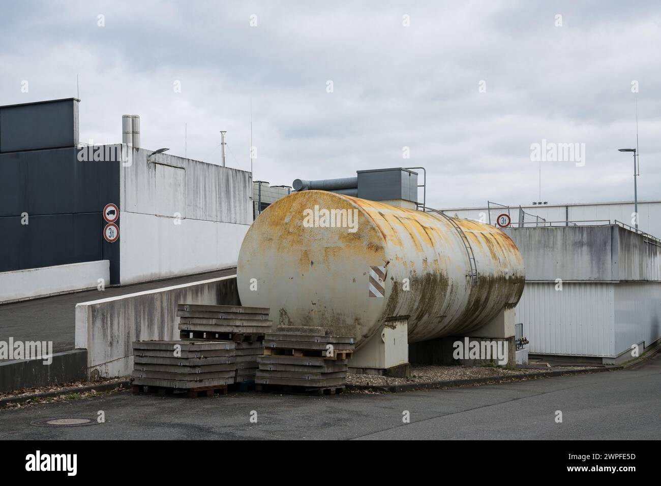 Large metal tank near an industrial building under a gray cloudy sky ...