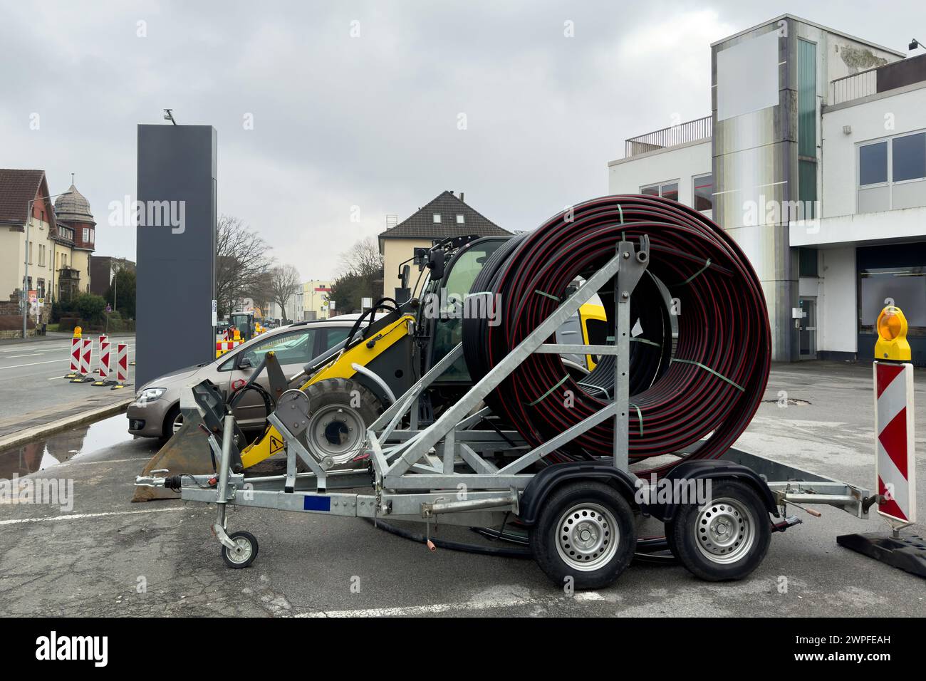 A reel with a cable wound on it in a car parking lot. Behind it is a ...