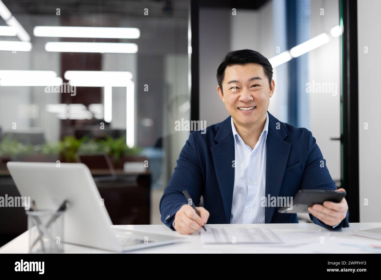 A happy Asian male professional in a blazer looks at the camera with ...