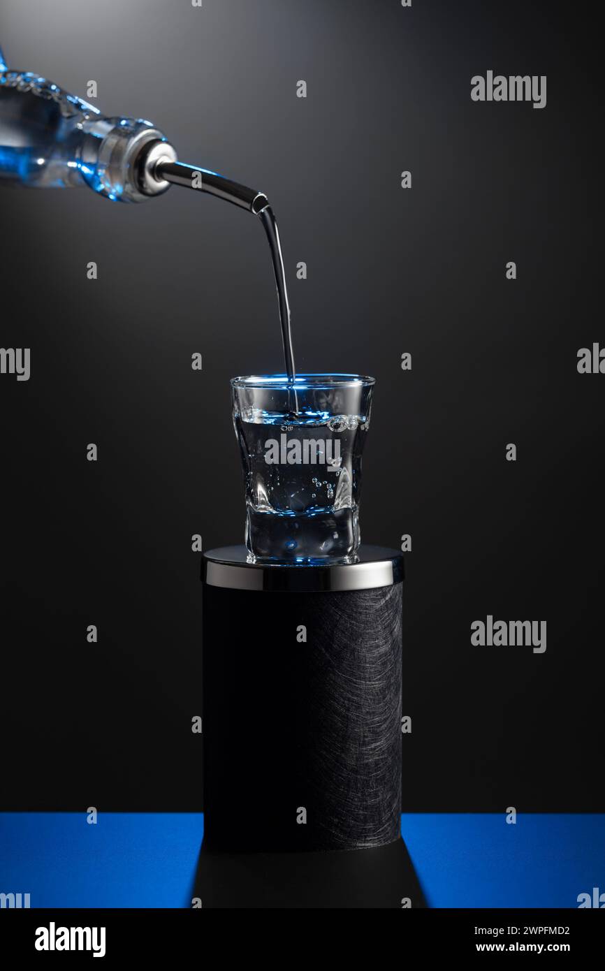 Vodka pouring from the bottle into a glass on a dark background. Blue ...