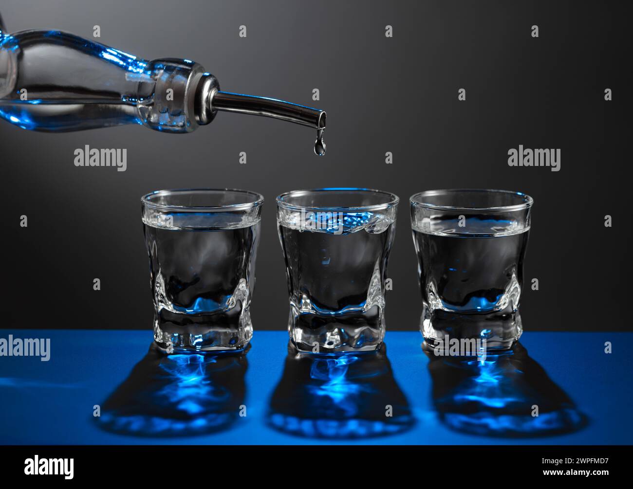 Vodka pouring from the bottle into a glass on a dark background. Blue ...