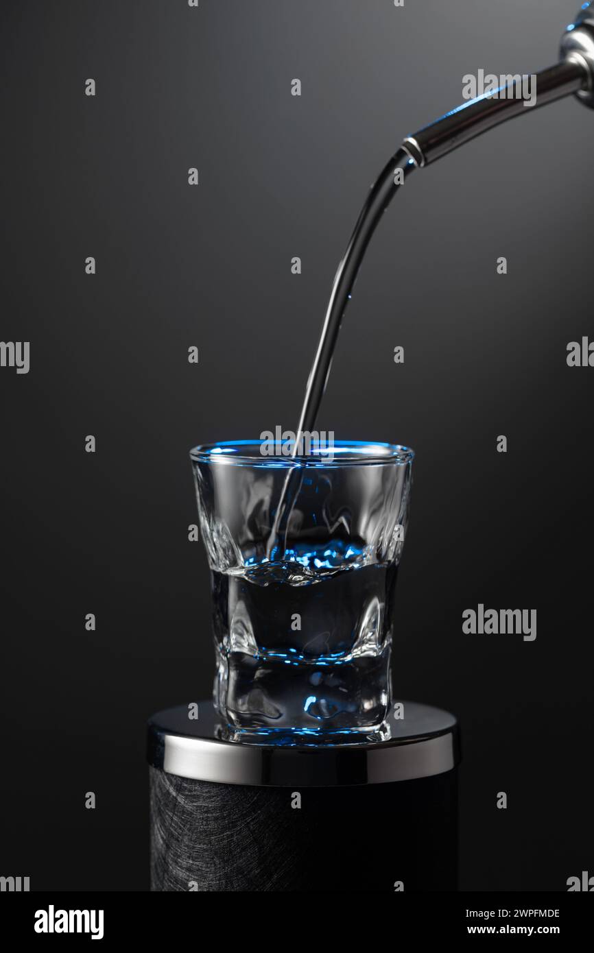 Vodka pouring from the bottle into a glass on a dark background. Blue ...