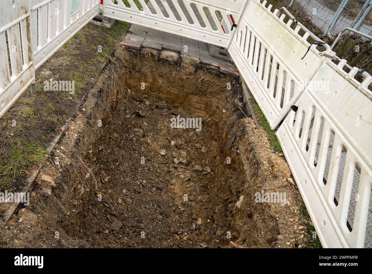 A dug trench fenced with white plastic barriers on a section of ...