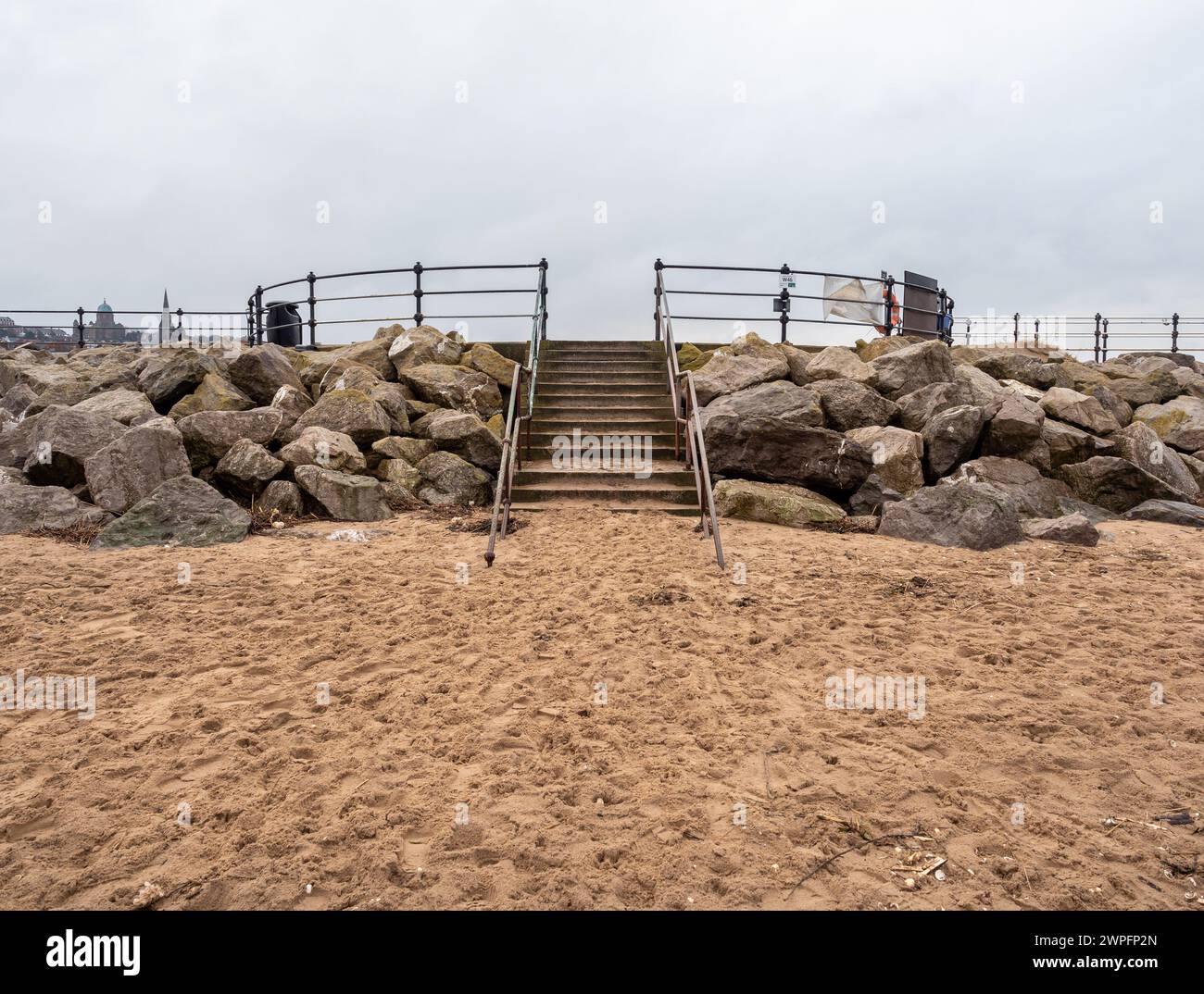 Stone steps up off the empty sandy beach up the sea wall onto the ...