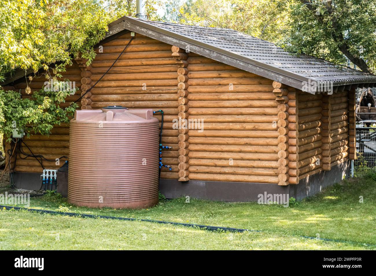 Neat log house with overflow barrel for outdoor pool filling in green ...