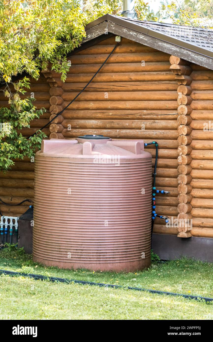 Neat log house with overflow barrel for outdoor pool filling in green ...