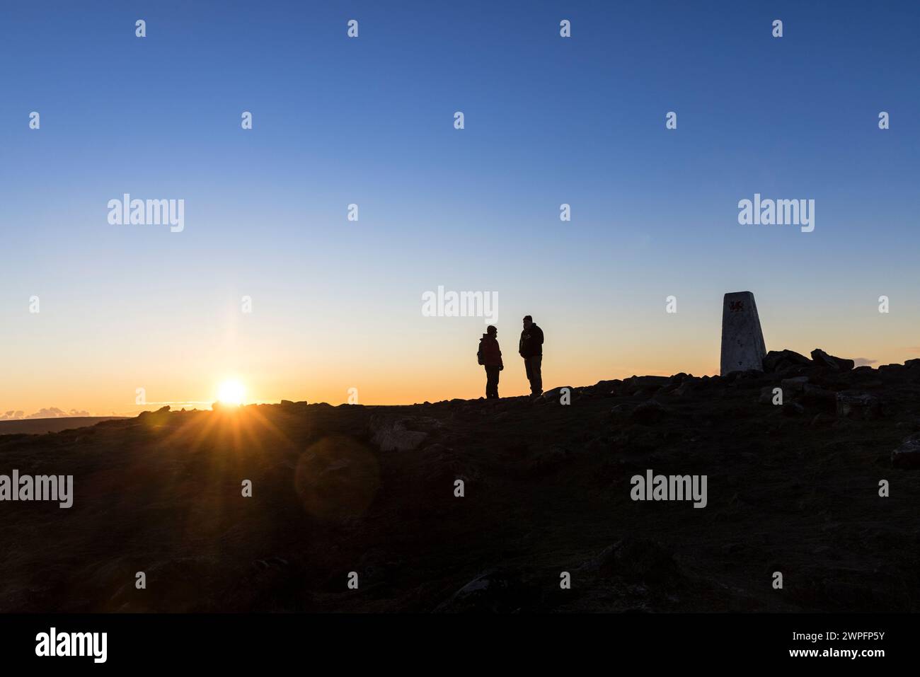 Two walkers silhouetted on skyline on the Blorenge mountain at sunset ...