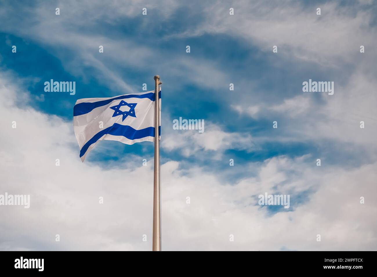 The Israeli flag with the Star of David waving against a cloudy blue ...