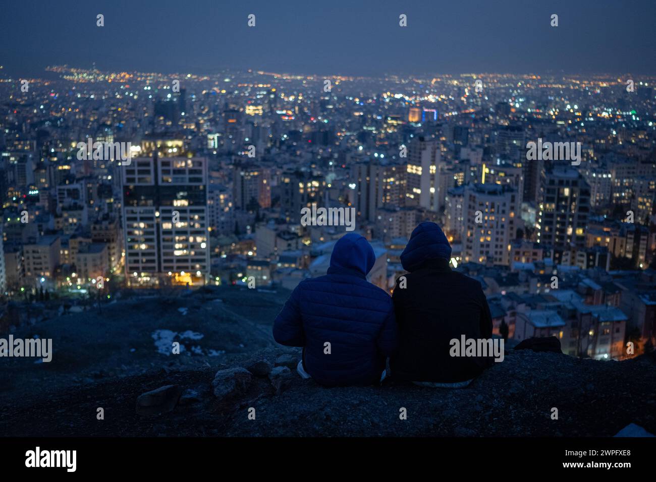 07 March 2024, Iran, Teheran: Two young men sit above the rooftops of ...