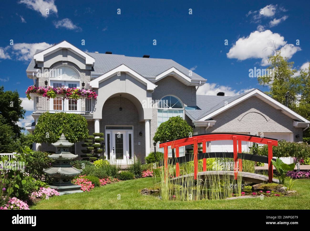 Grey brick with white trim two story home and red wooden footbridge ...