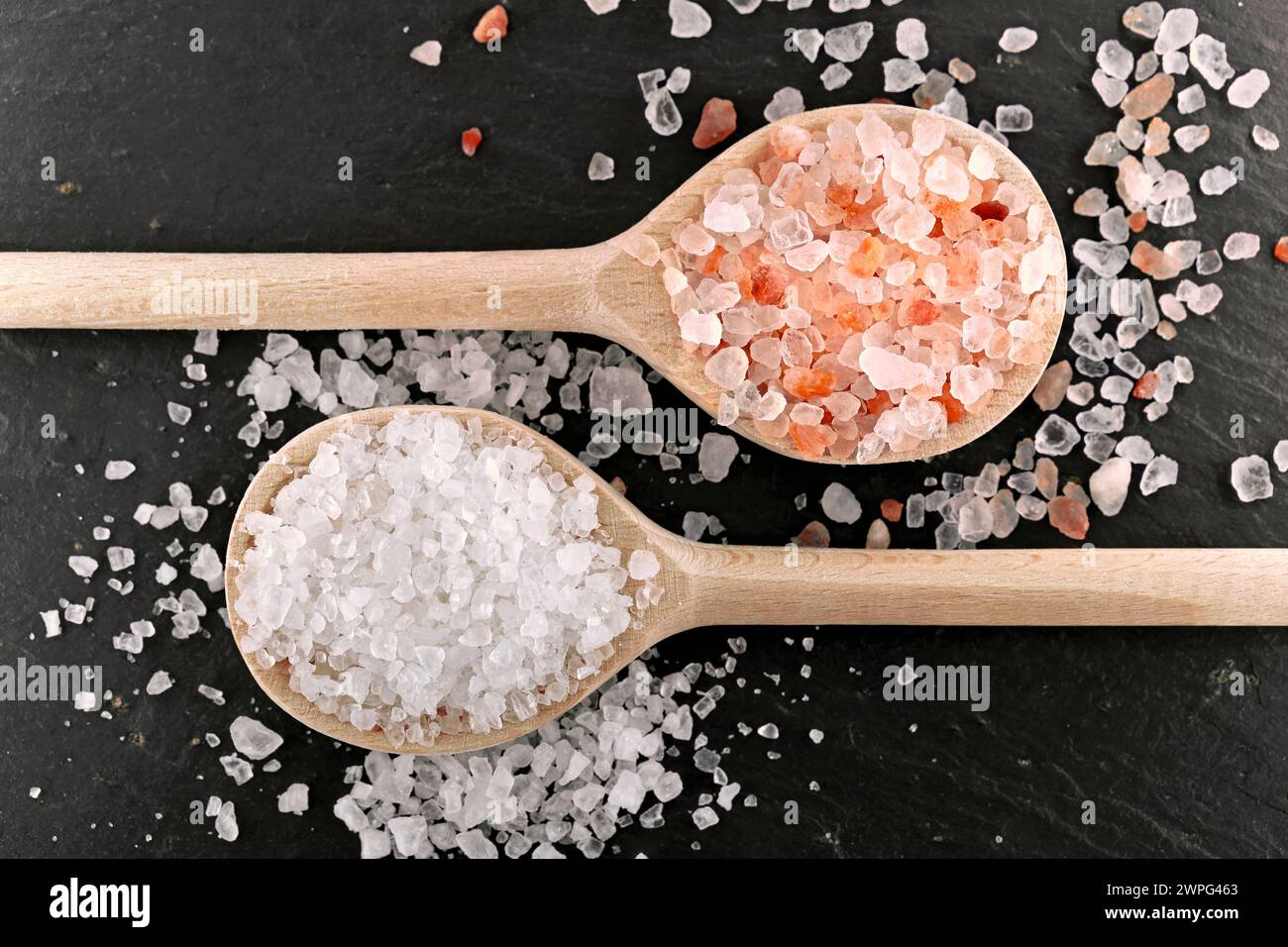 two different types of coarse salt on wooden cooking spoons on black ...