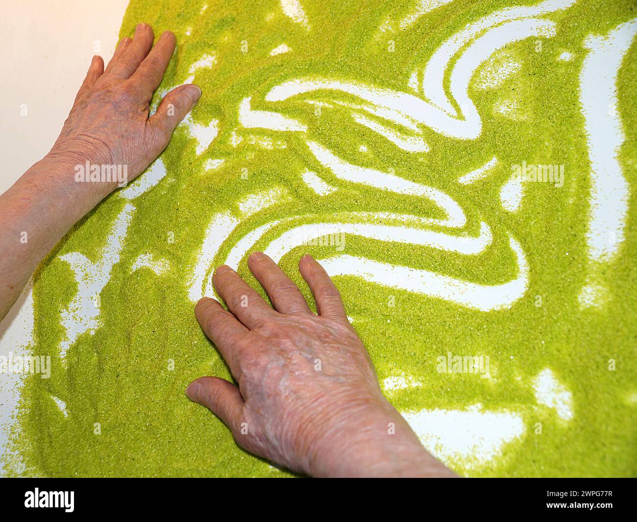 hands of an elderly woman on a white table with green sand, sand ...