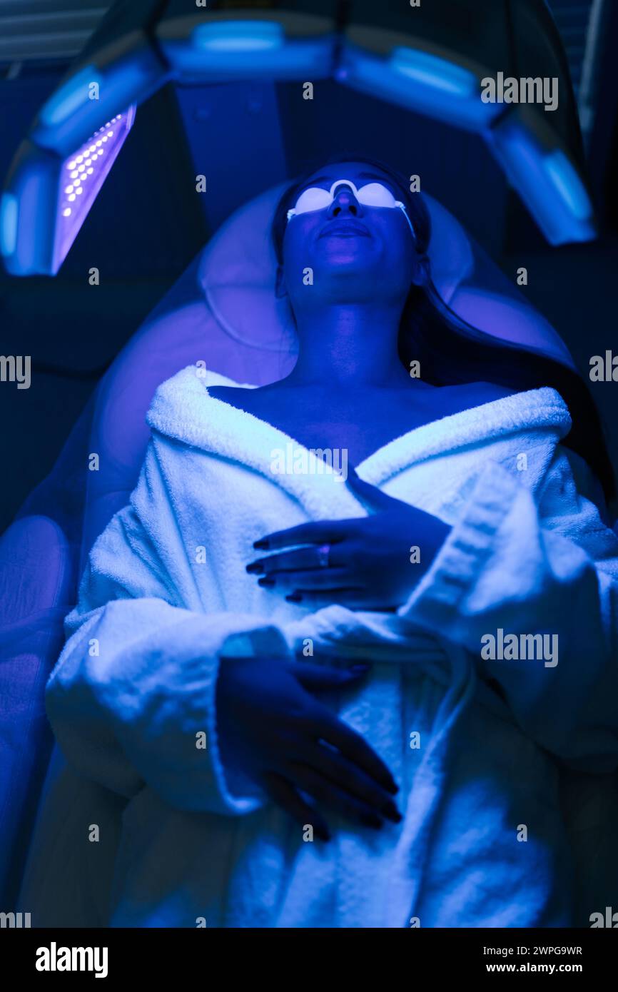 Vertical portrait of female patient undergoes blue LED light therapy ...