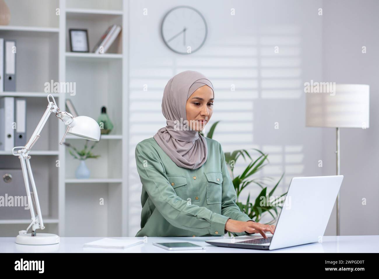 Focused Muslim woman in hijab at work on her laptop in a well-lit ...