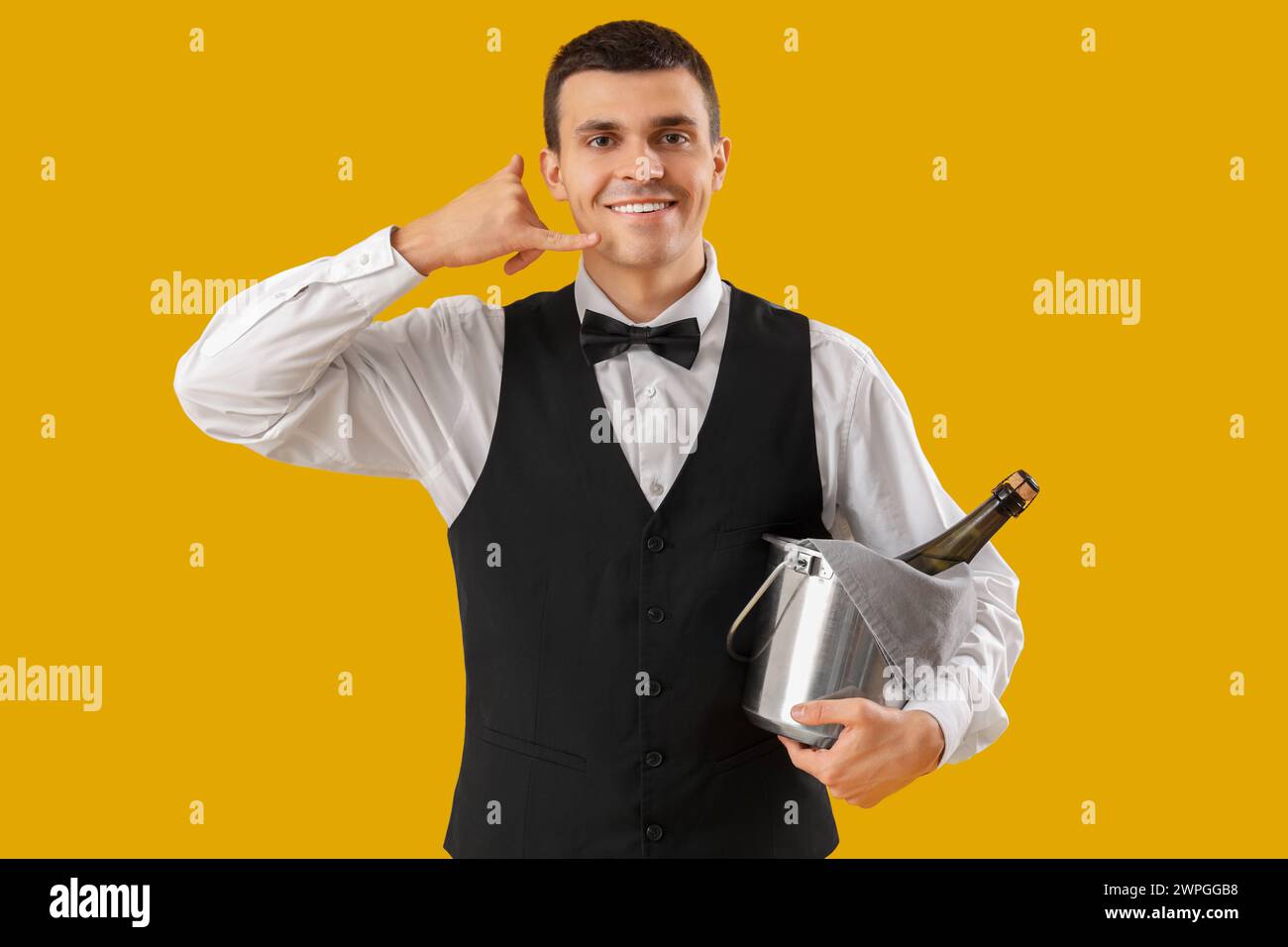 Male waiter with champagne showing "call me" gesture on yellow ...