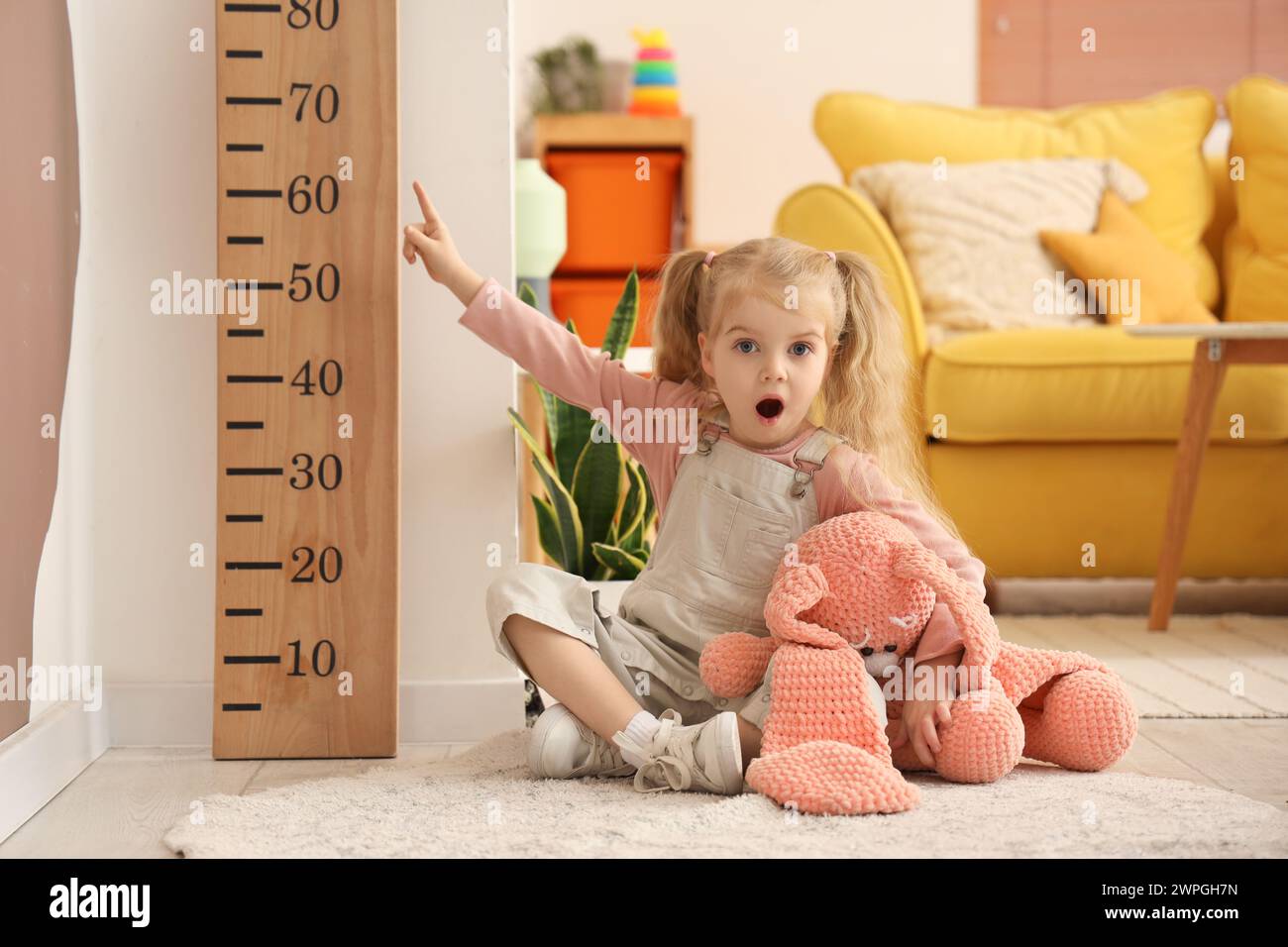 Surprised little girl with toy pointing at wooden stadiometer in ...