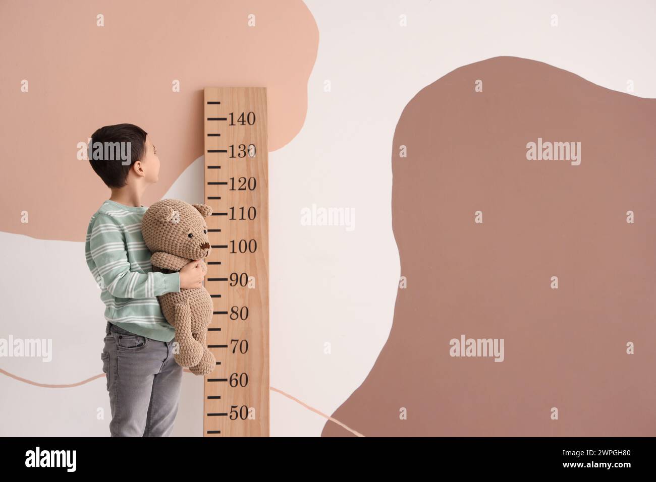 Cute little boy with toy measuring height near wooden stadiometer at ...
