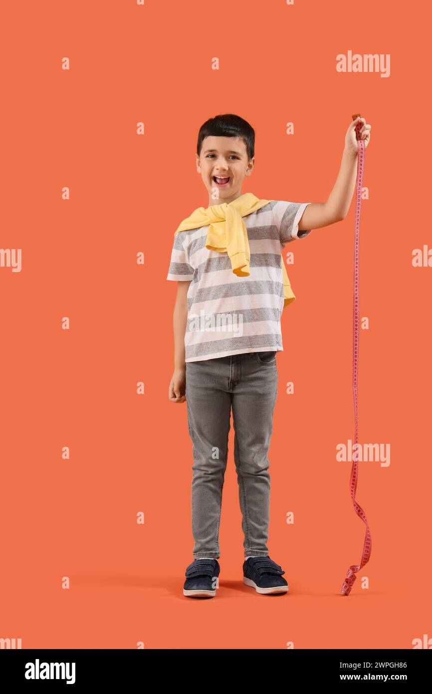 Cute little boy measuring height with tape on orange background Stock ...