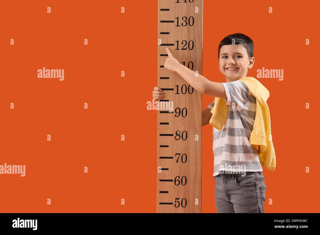 Cute little boy measuring height near wooden stadiometer on orange ...
