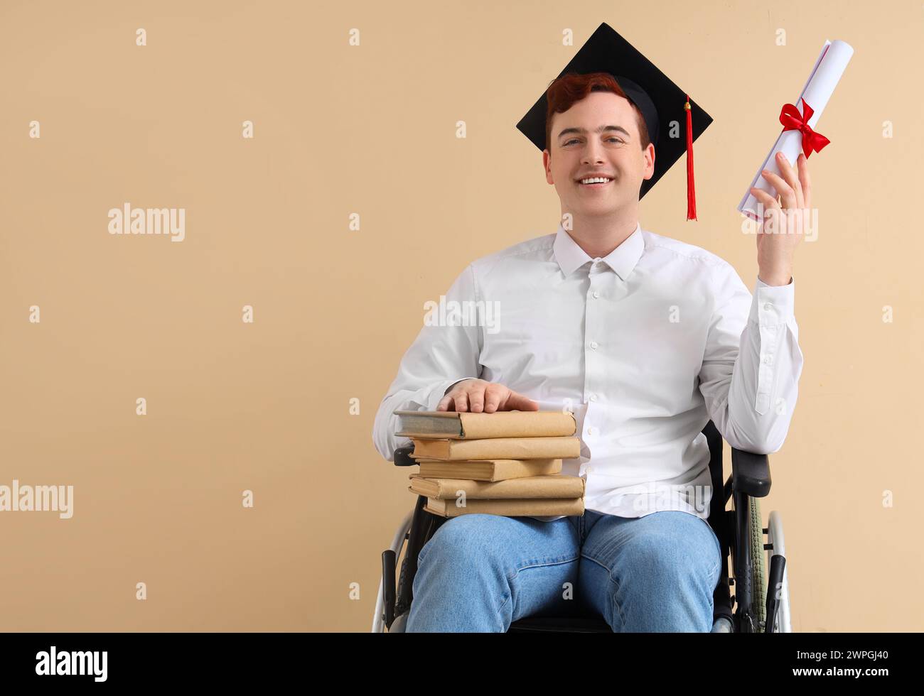 Male graduate in wheelchair with diploma and books on beige background ...