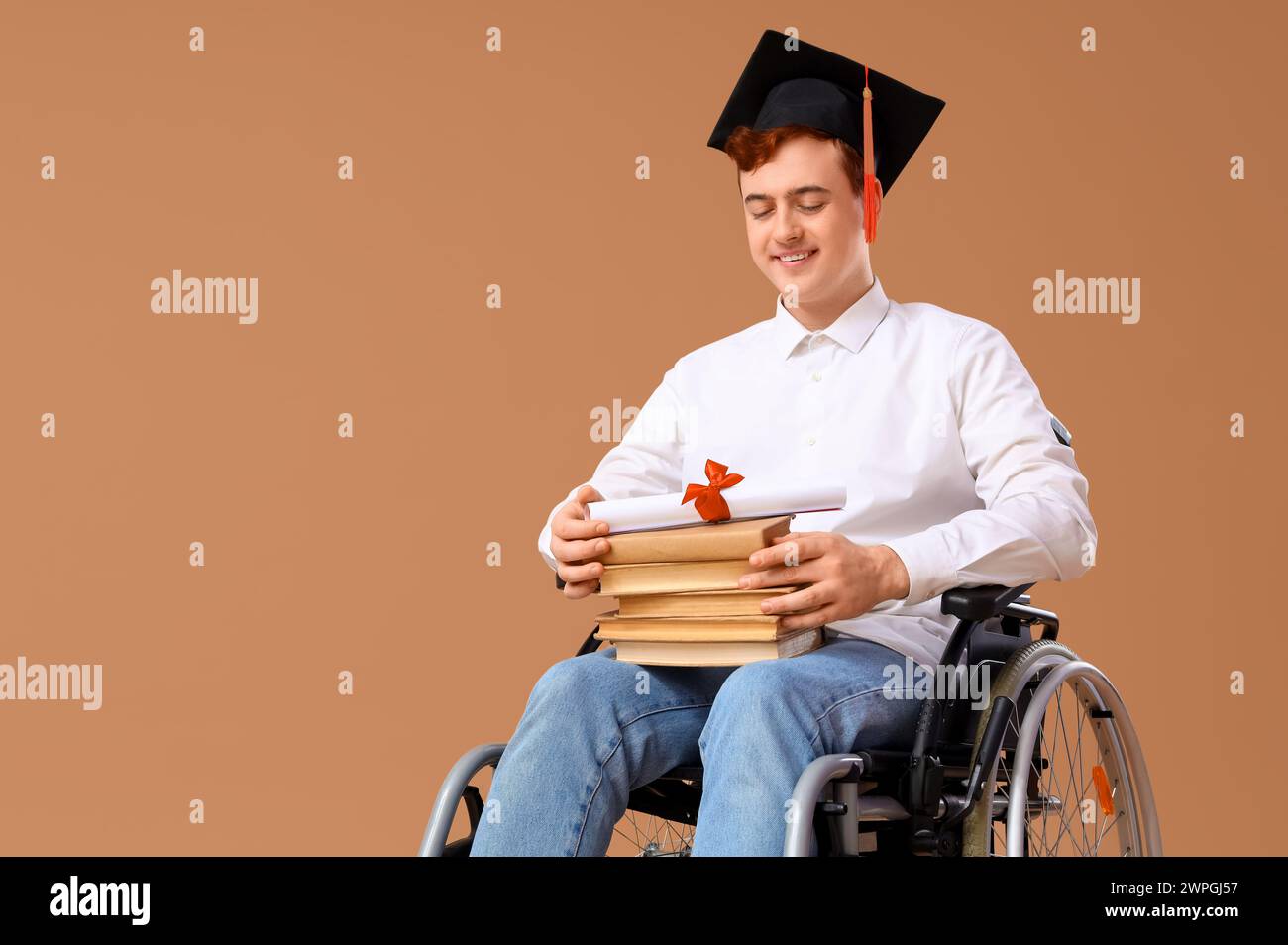 Male graduate in wheelchair with diploma and books on beige background ...