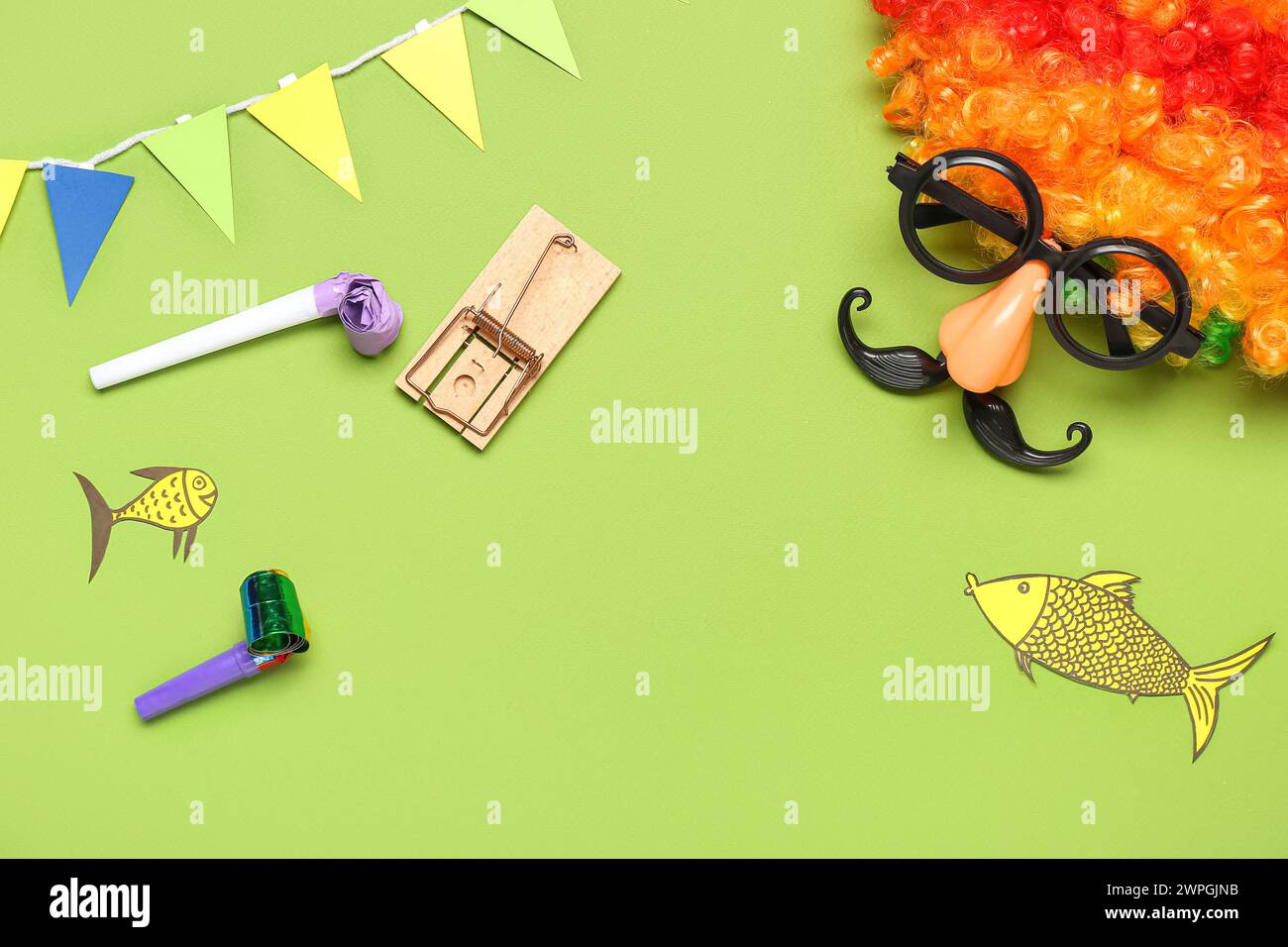 Clown wig with funny glasses, mousetrap and paper fishes on green ...
