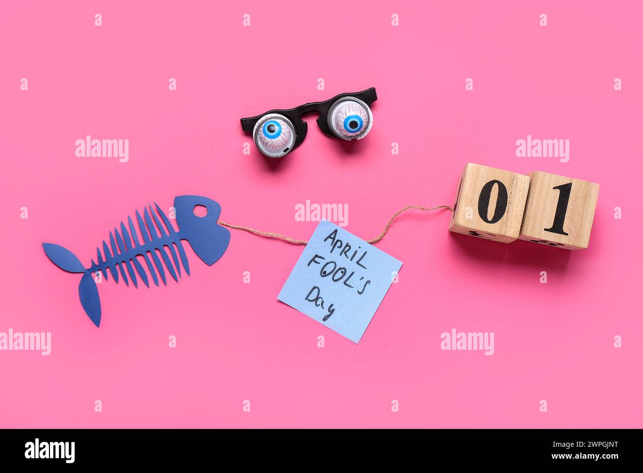 Cubes with funny glasses, paper fish and sticky note on pink background ...