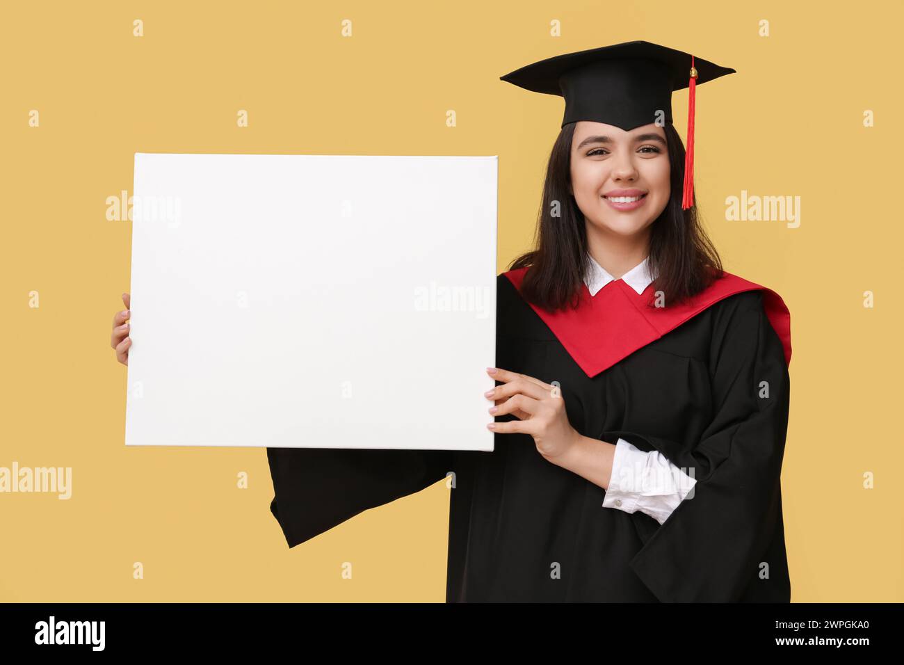 Happy female graduating student with blank poster on yellow background ...