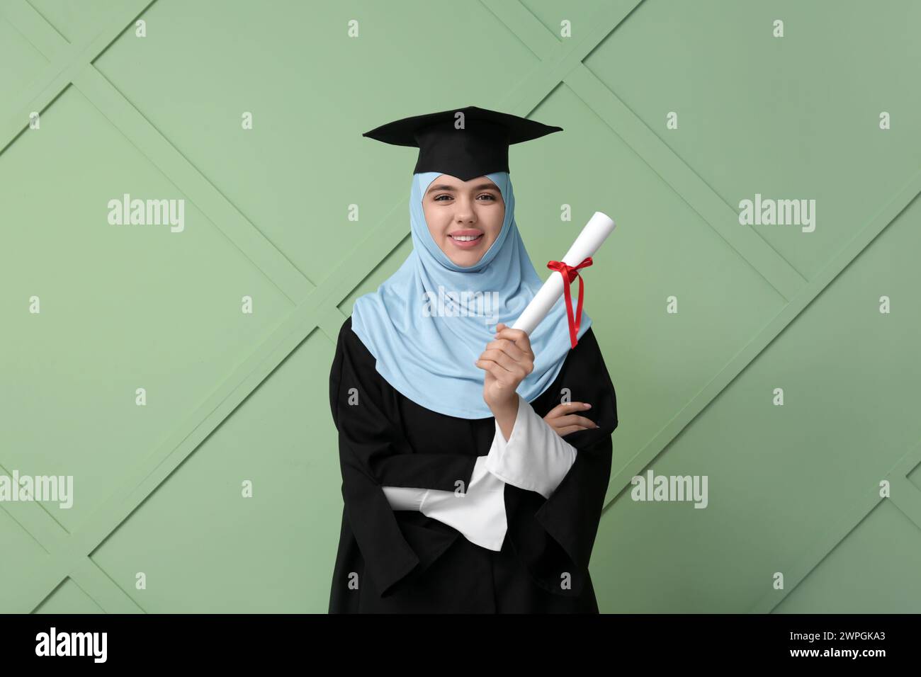 Happy Muslim female graduating student with diploma on green wooden ...