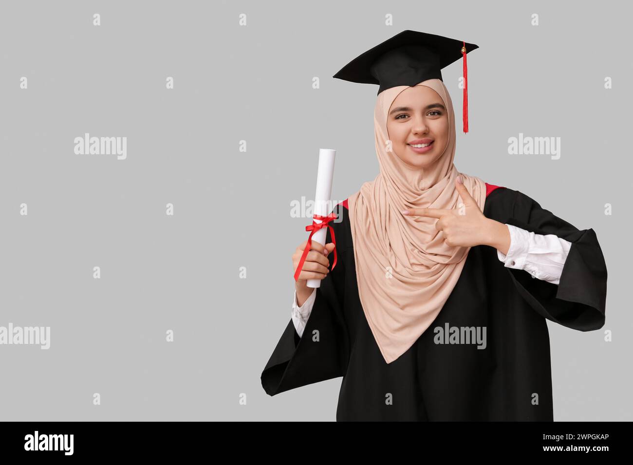 Happy Muslim female graduating student pointing at diploma on white ...